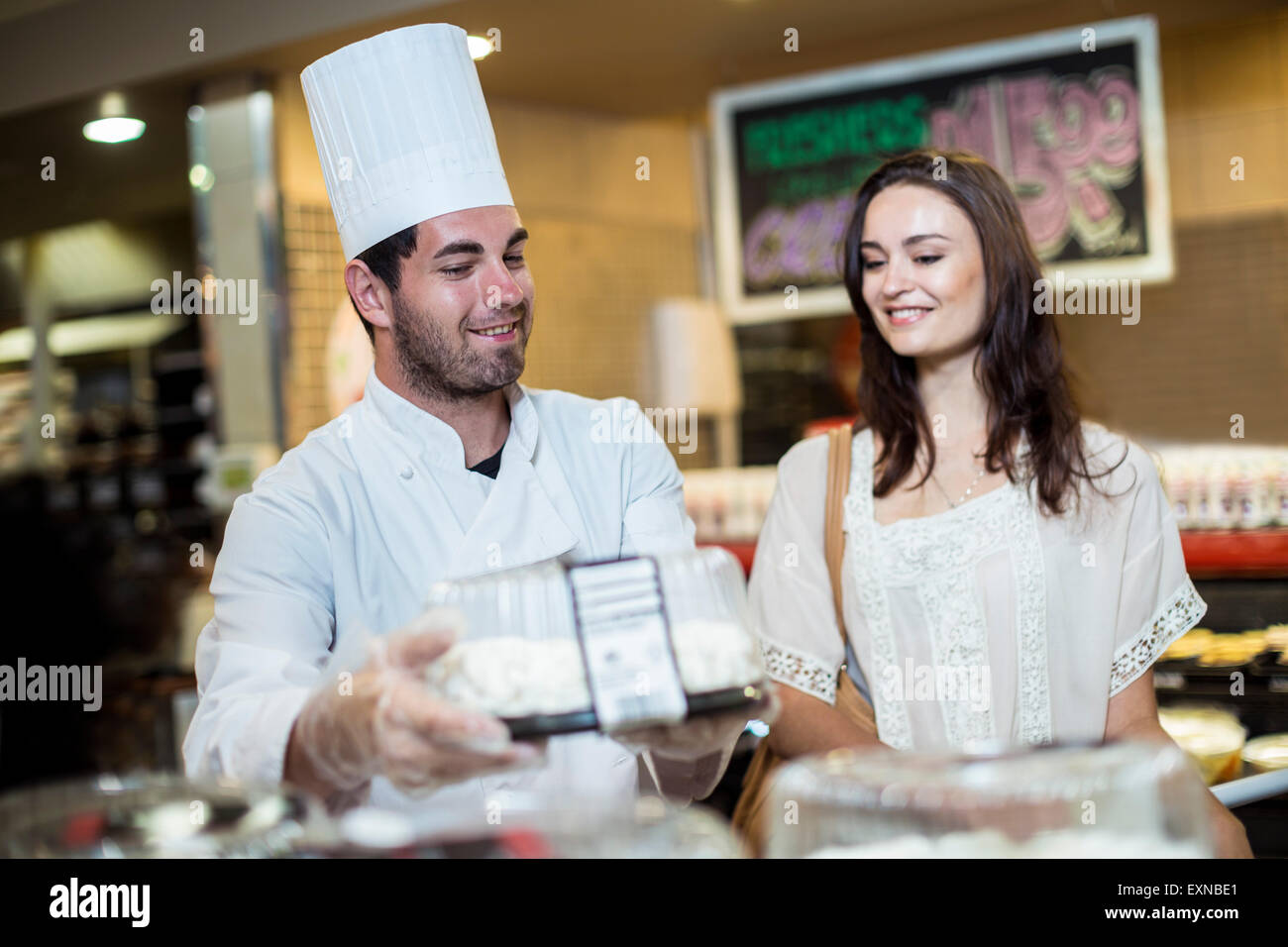 Male chef in bakery helping female client in supermarket Stock Photo ...