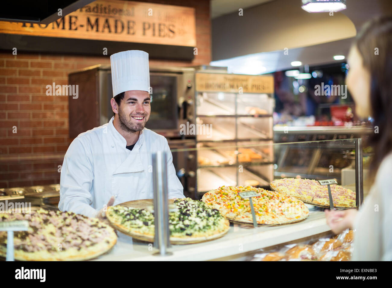 Male chef in bakery serving pizza to female client Stock Photo - Alamy