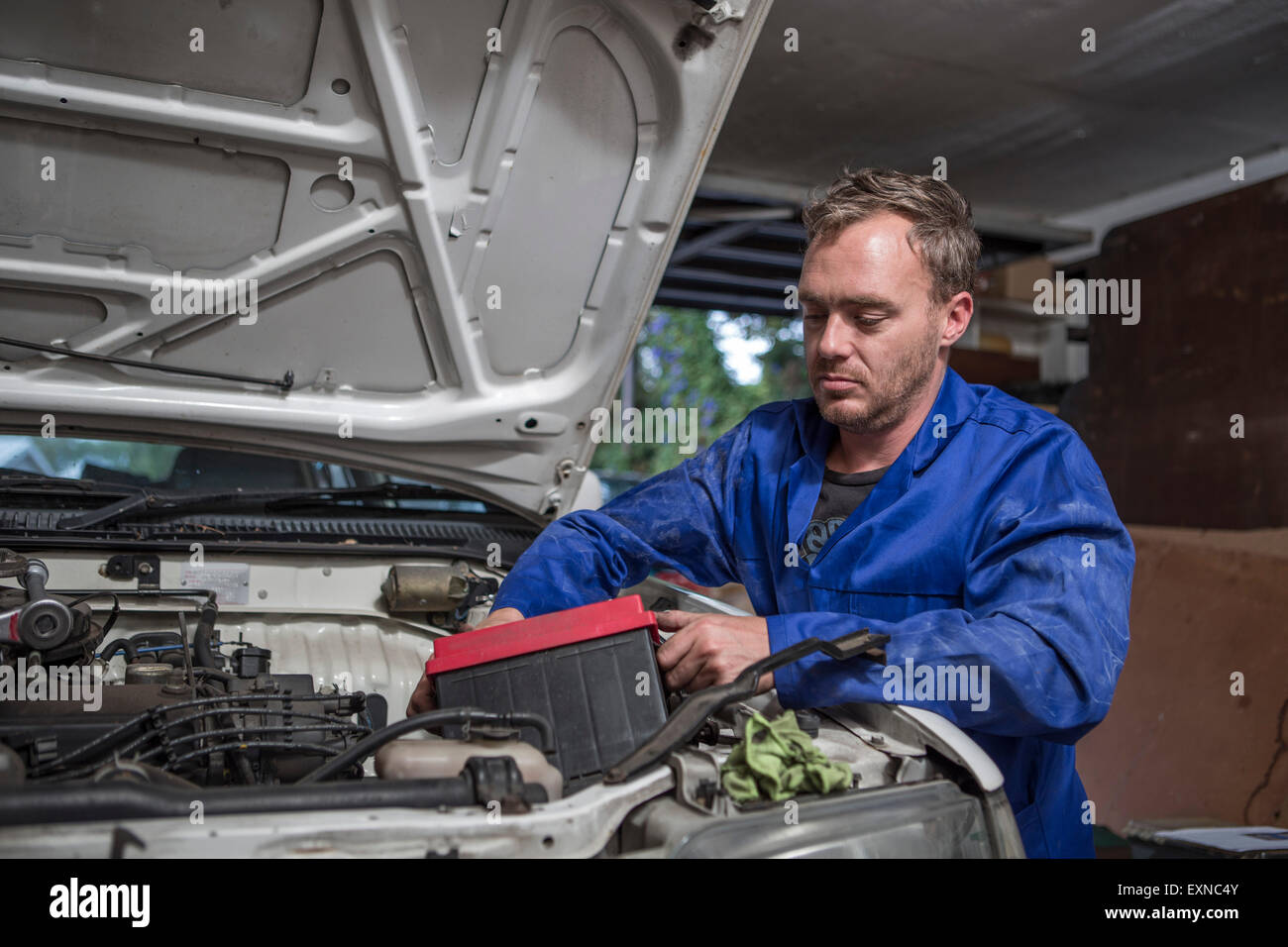 Man working on car in home garage removing battery Stock Photo - Alamy