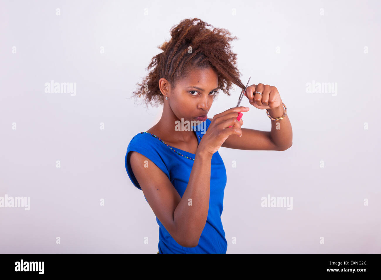 Young African American woman cutting her frizzy afro hair with scissors ...