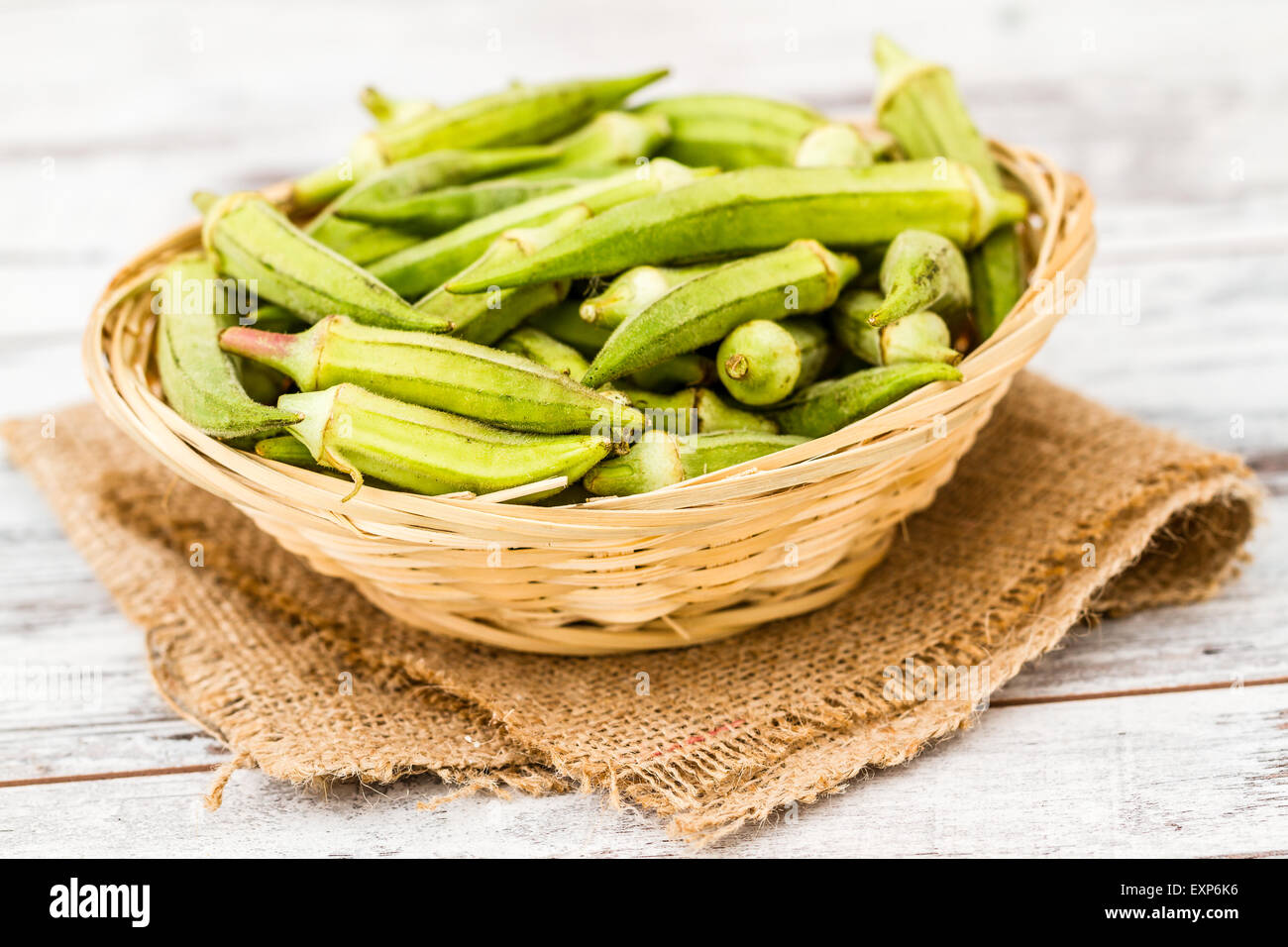 Green okra vegetable on linen napkin against white wooden background ...