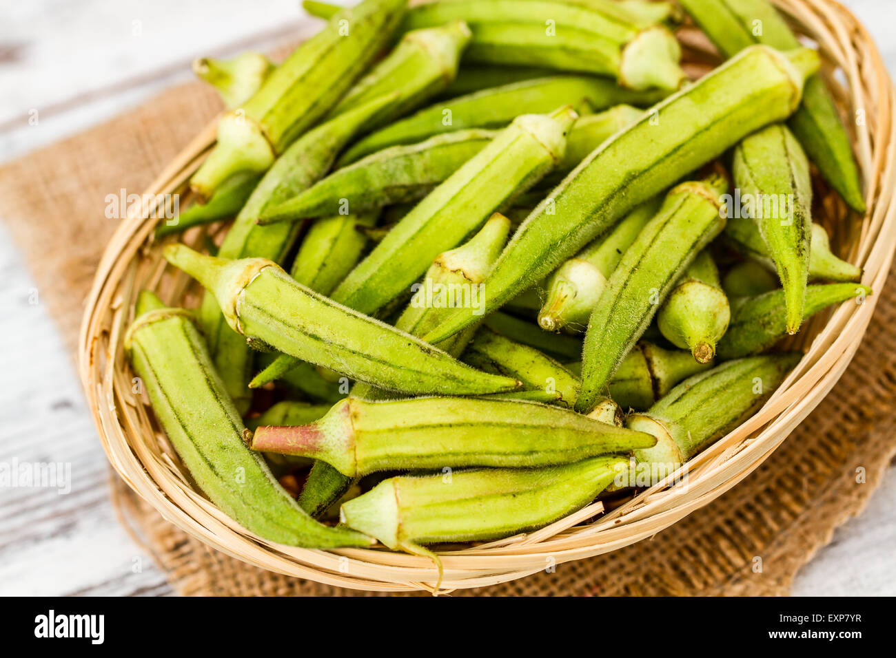 Green okra vegetable on linen napkin against white wooden background ...
