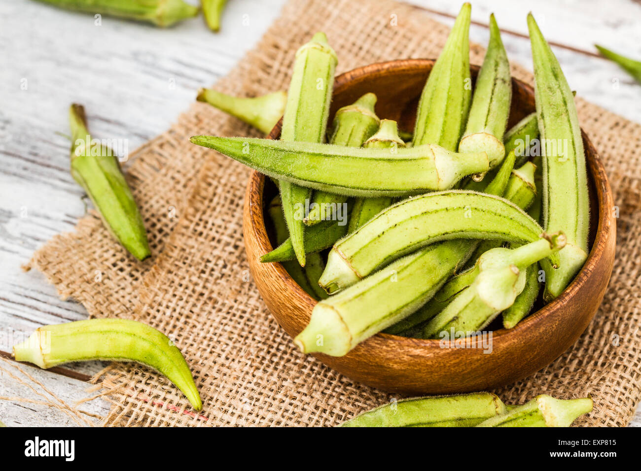 Green okra vegetable on linen napkin against white wooden background ...