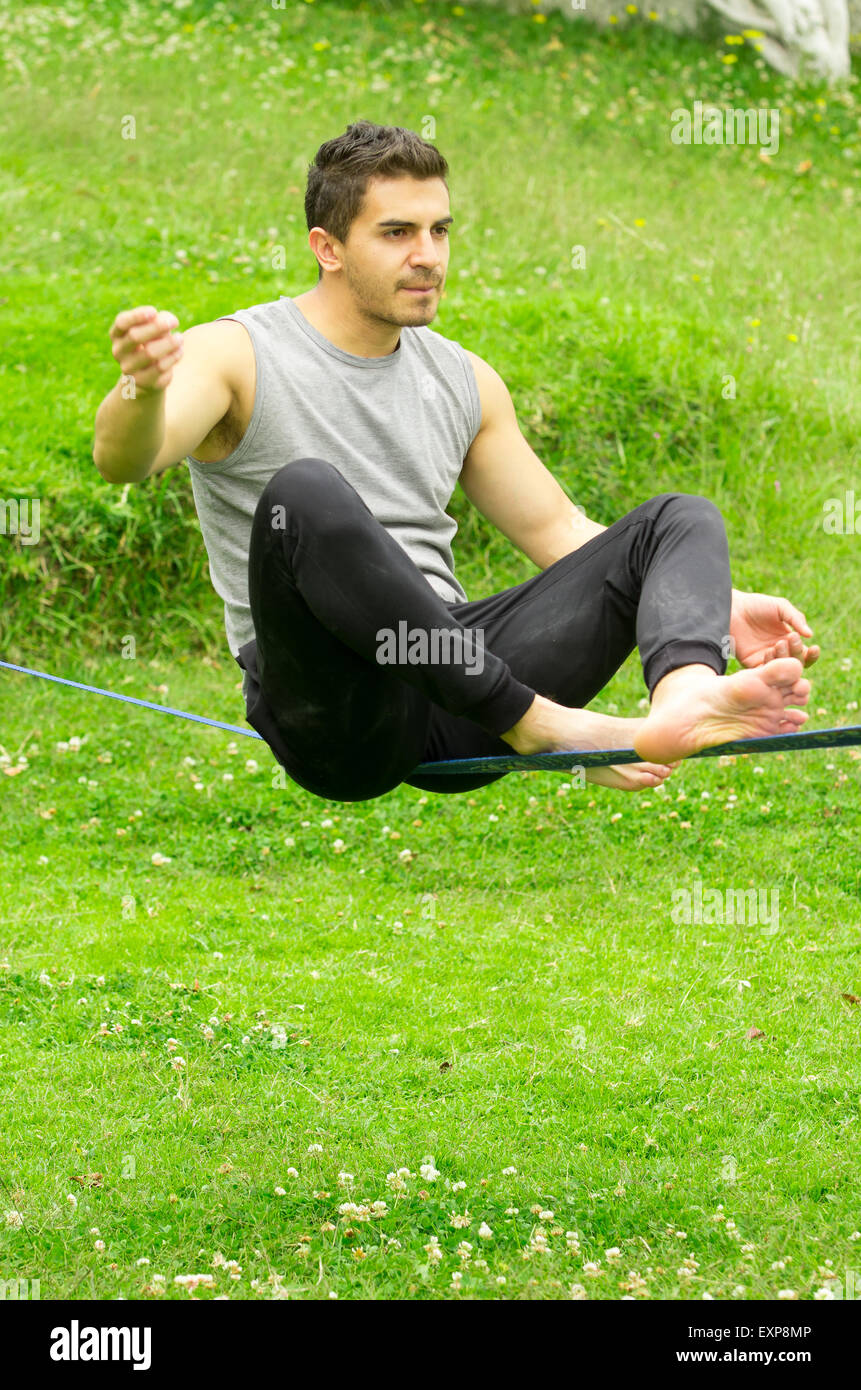 Man sitting on slackline concentrating to keep balance with grassy ...