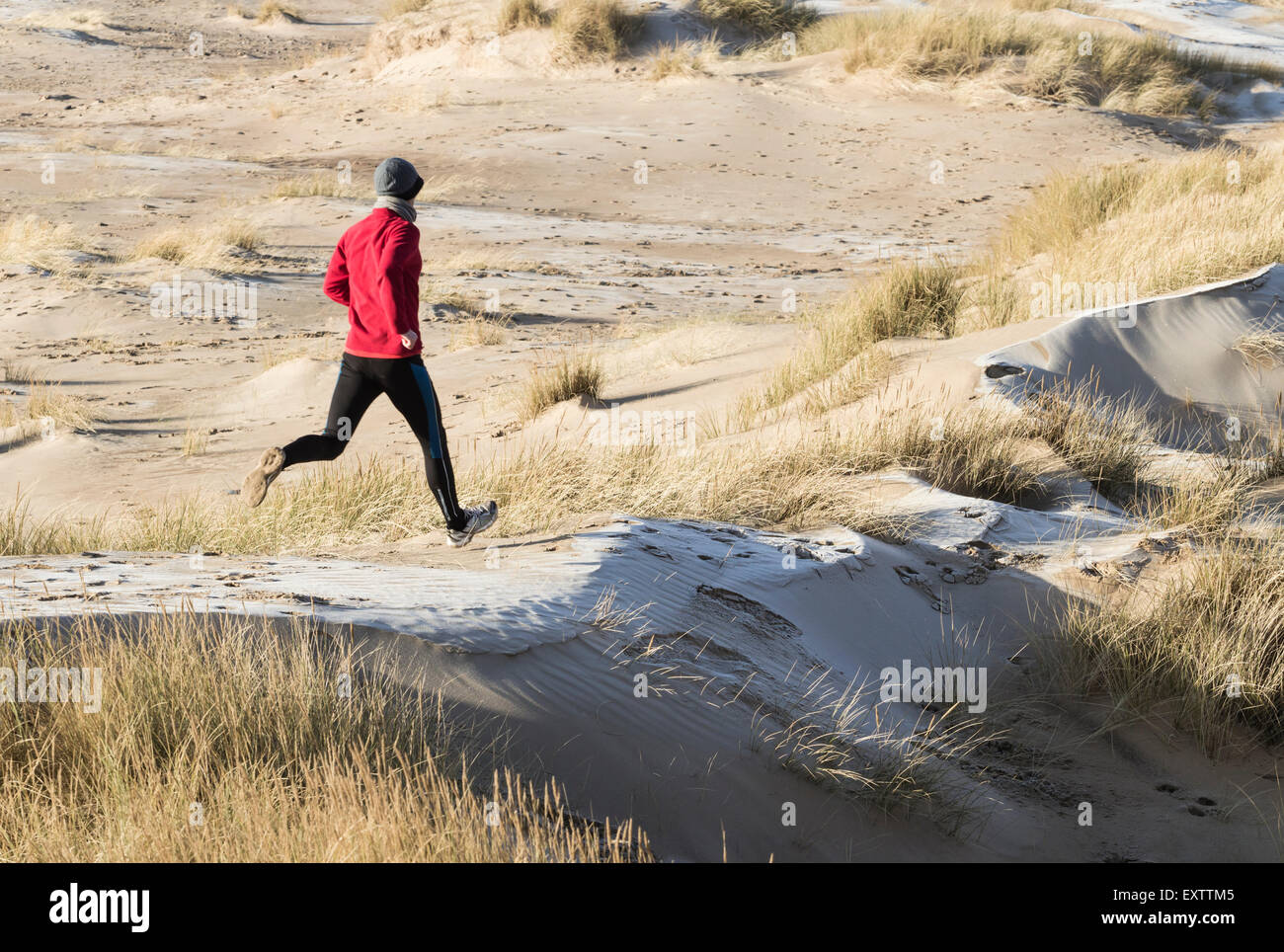Mature man running on sand dunes covered in frost at Seaton Carew on ...