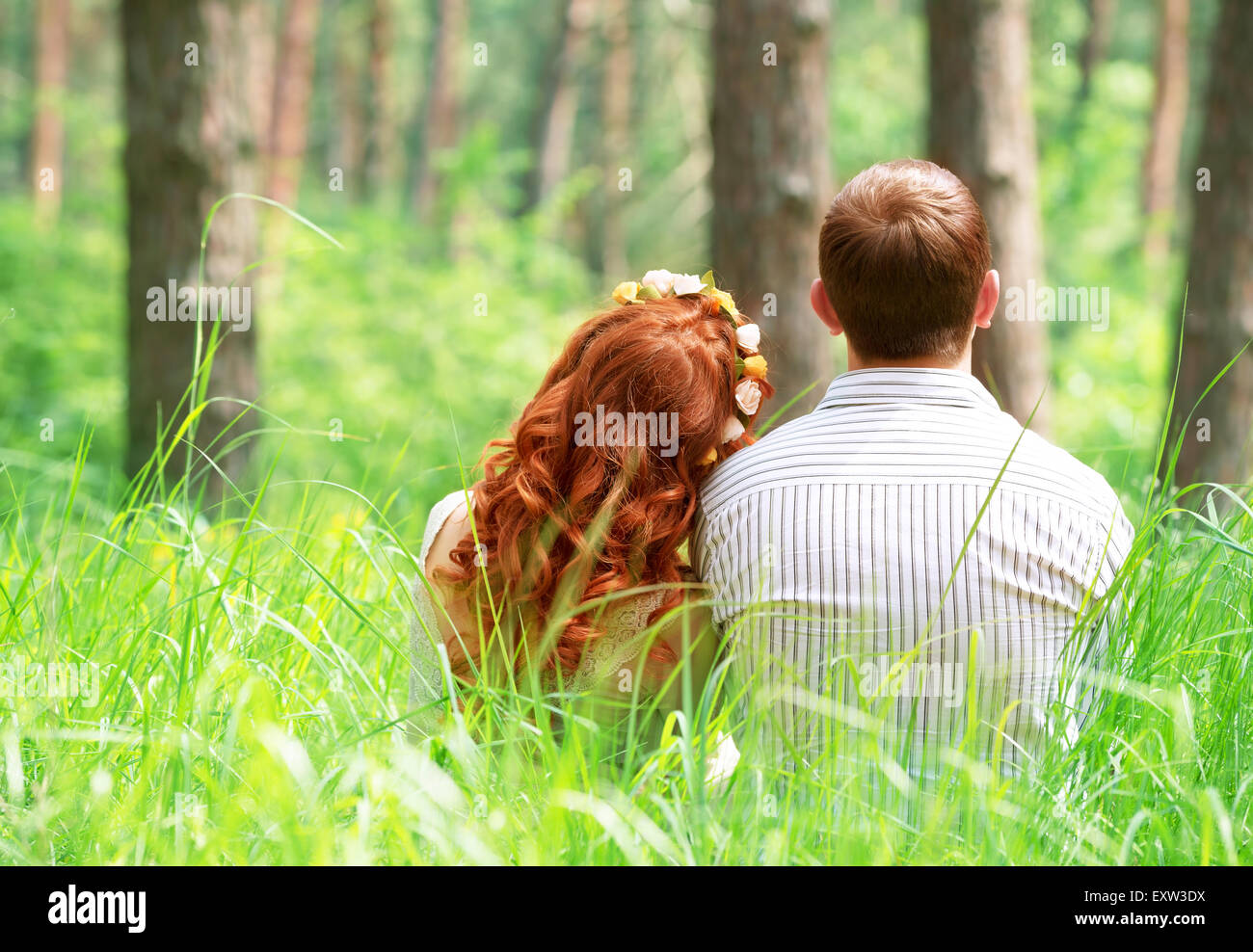 Back side of cute peaceful couple sitting on grass in the park ...