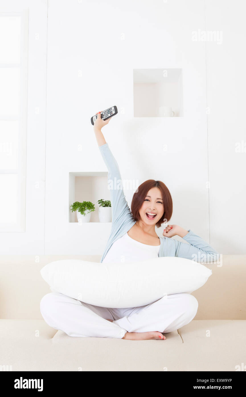 Young woman sitting on the sofa and holding remote control with smile ...