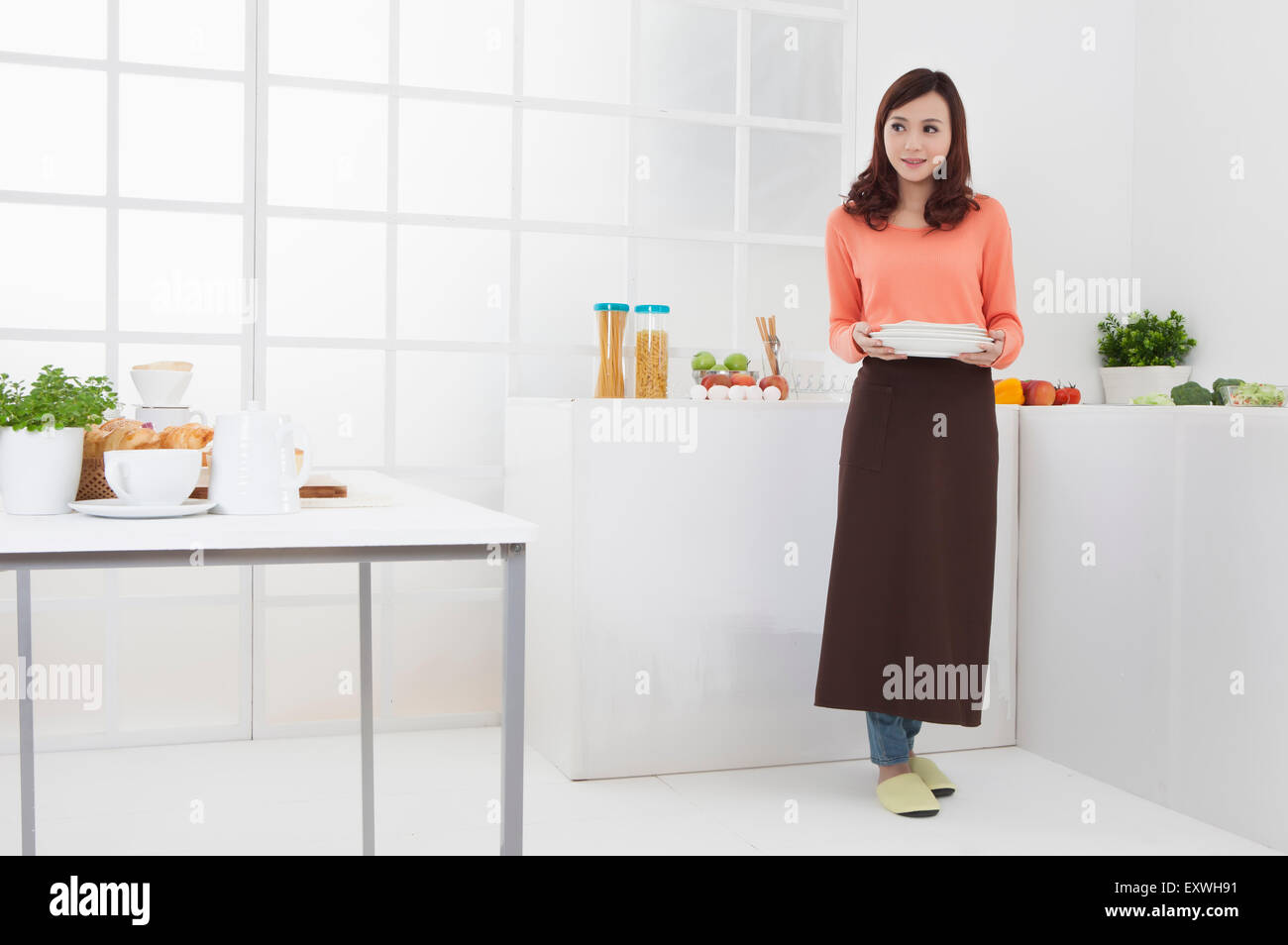Young woman holding plates and standing in the kitchen Stock Photo - Alamy