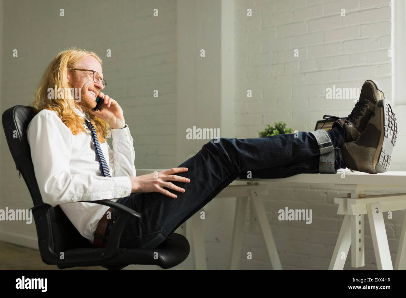 Man talking on phone with feet up on desk Stock Photo - Alamy