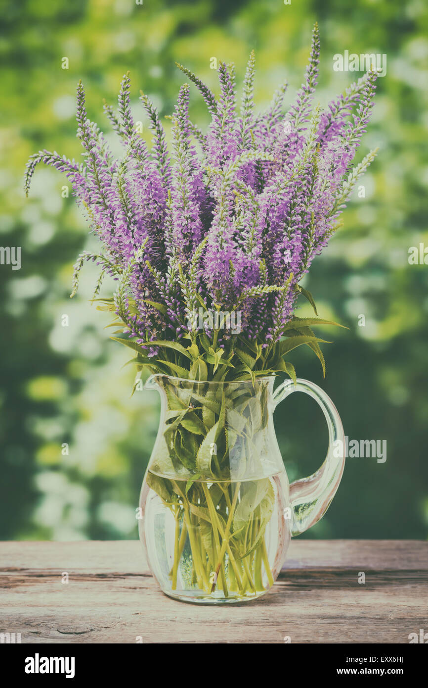 Bunch of wild flowers in a jug on old wooden table. Vintage stylized ...