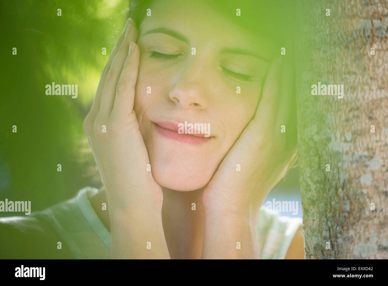 Woman Leanng Against Tree Trunk With Hands On Cheecks Eyes Closed