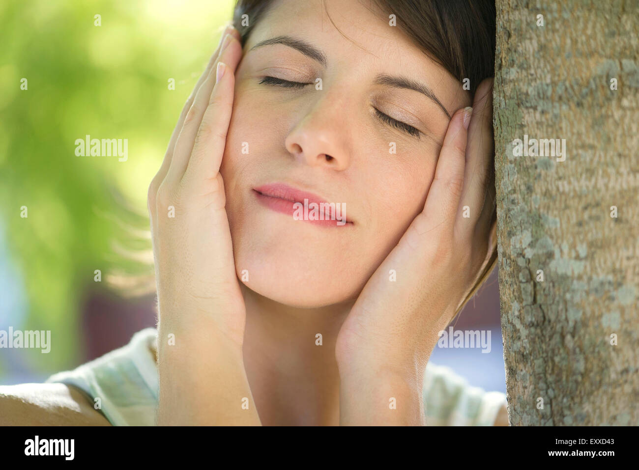Woman Leaning Against Tree Trunk With Hands On Cheeks Eyes Closed