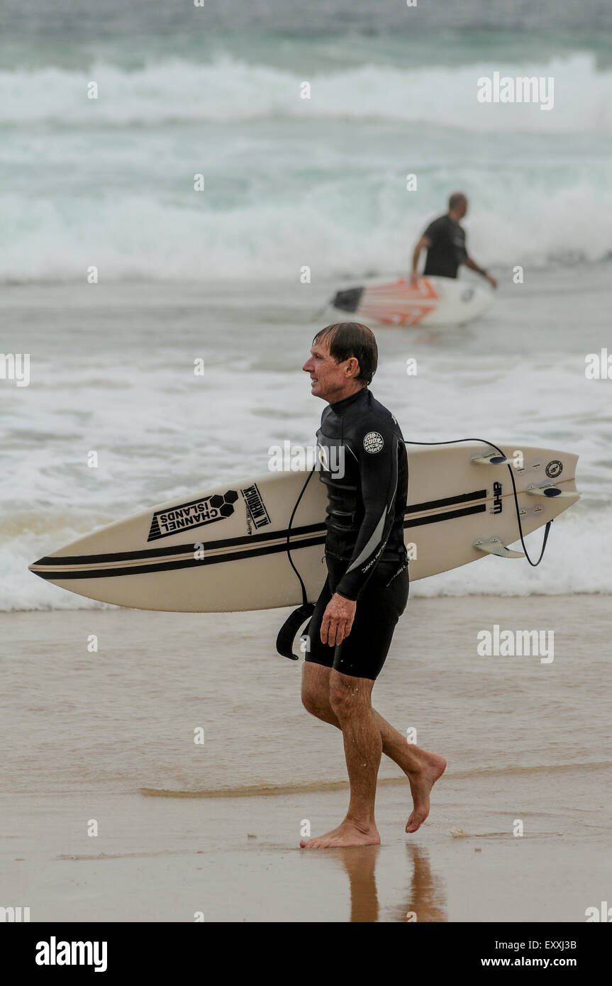 Two men walk oppisite directions with their surf boards at a beach in ...