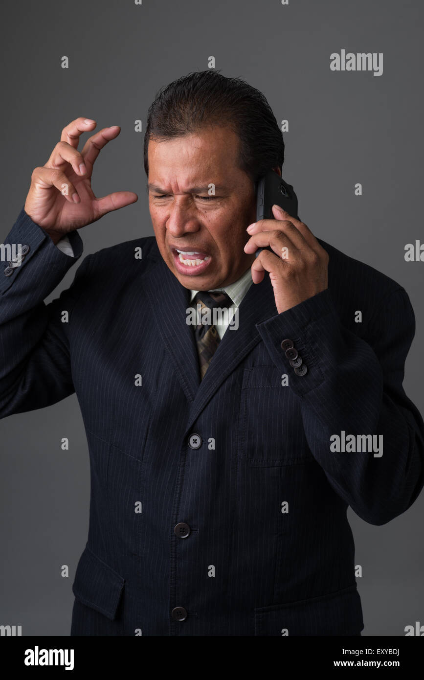A Hispanic businessman talking on his cell phone, angry and frustrated ...
