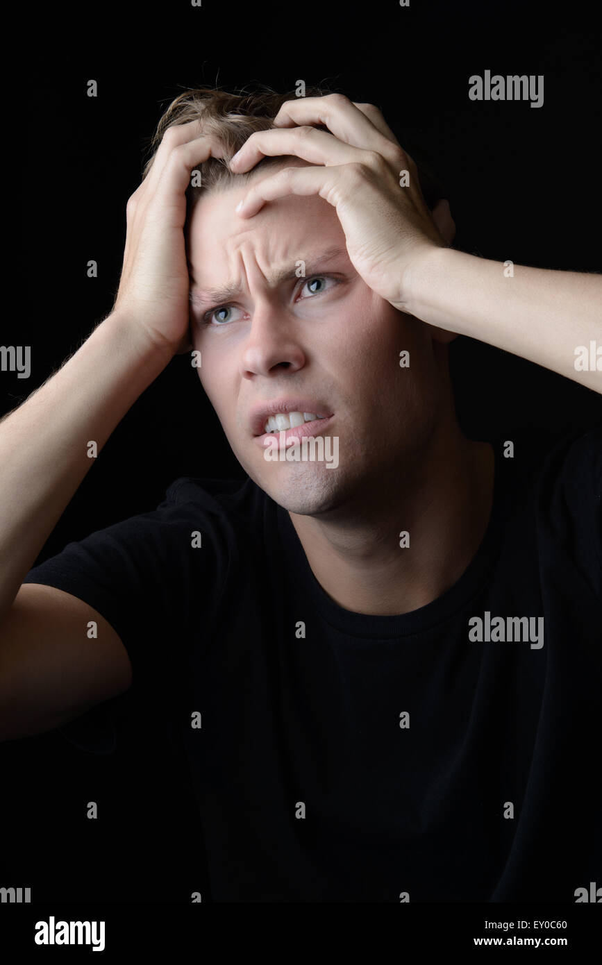 A young Caucasian man frustrated, angry and confused, grabbing his head ...