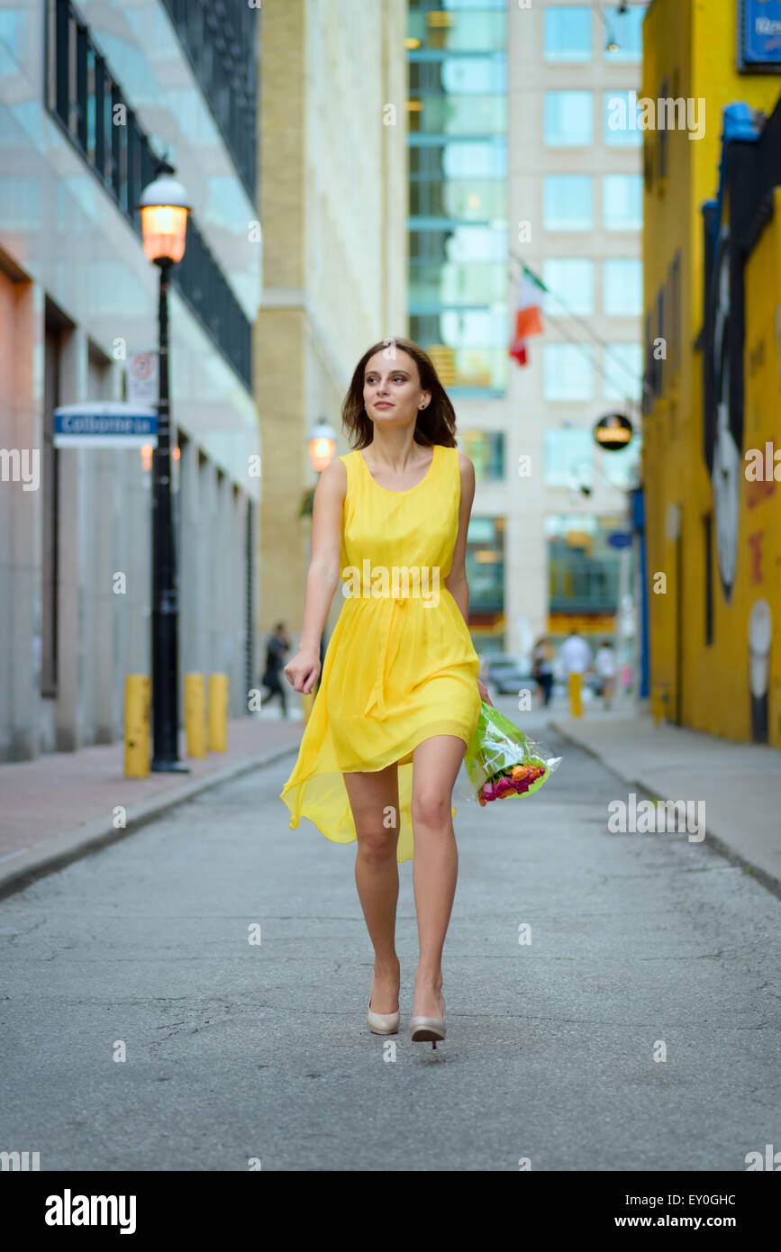 Beautiful young lady in yellow summer dress and with bunch of flowers ...