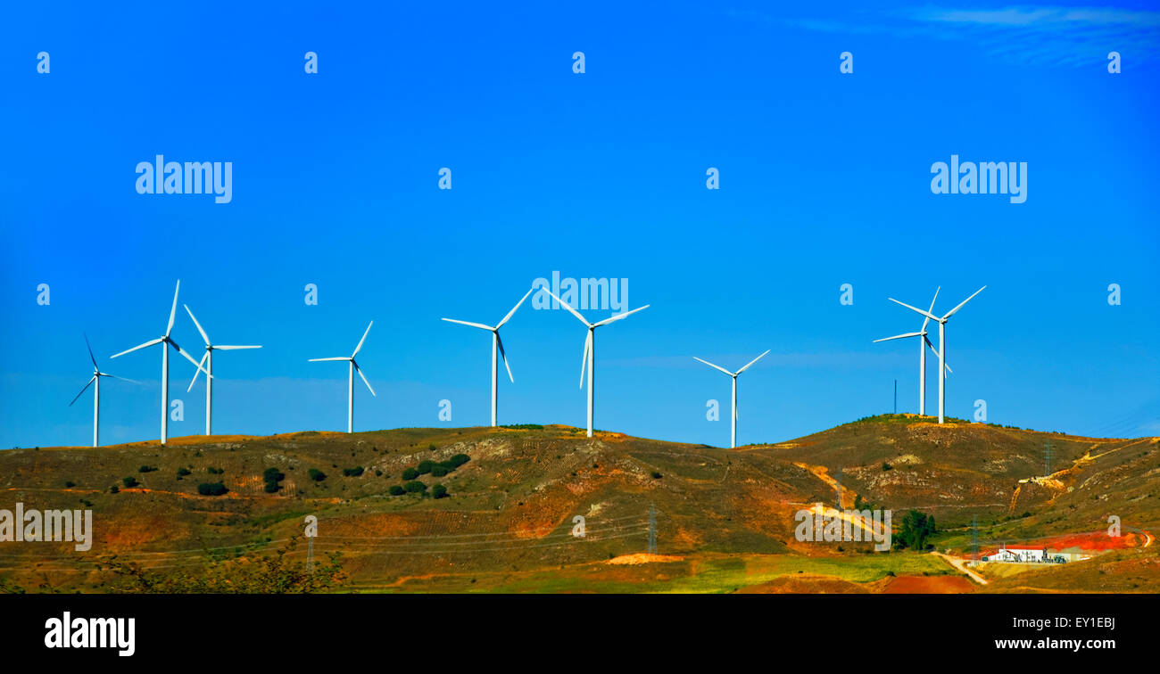 Wind turbines and power lines and poles on the hill in front of blue ...