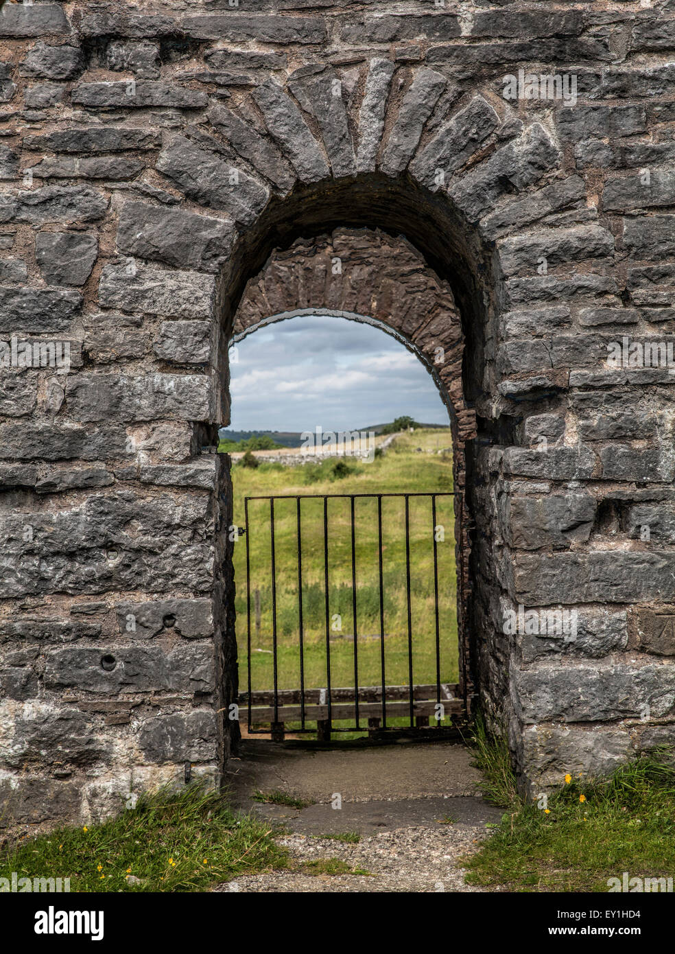 Stone arch and wall with a metal grill looking out to the fields of the ...