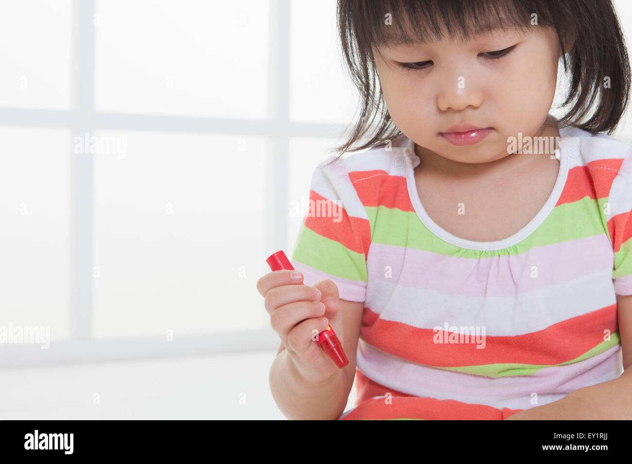 Little girl holding crayon and looking down Stock Photo - Alamy