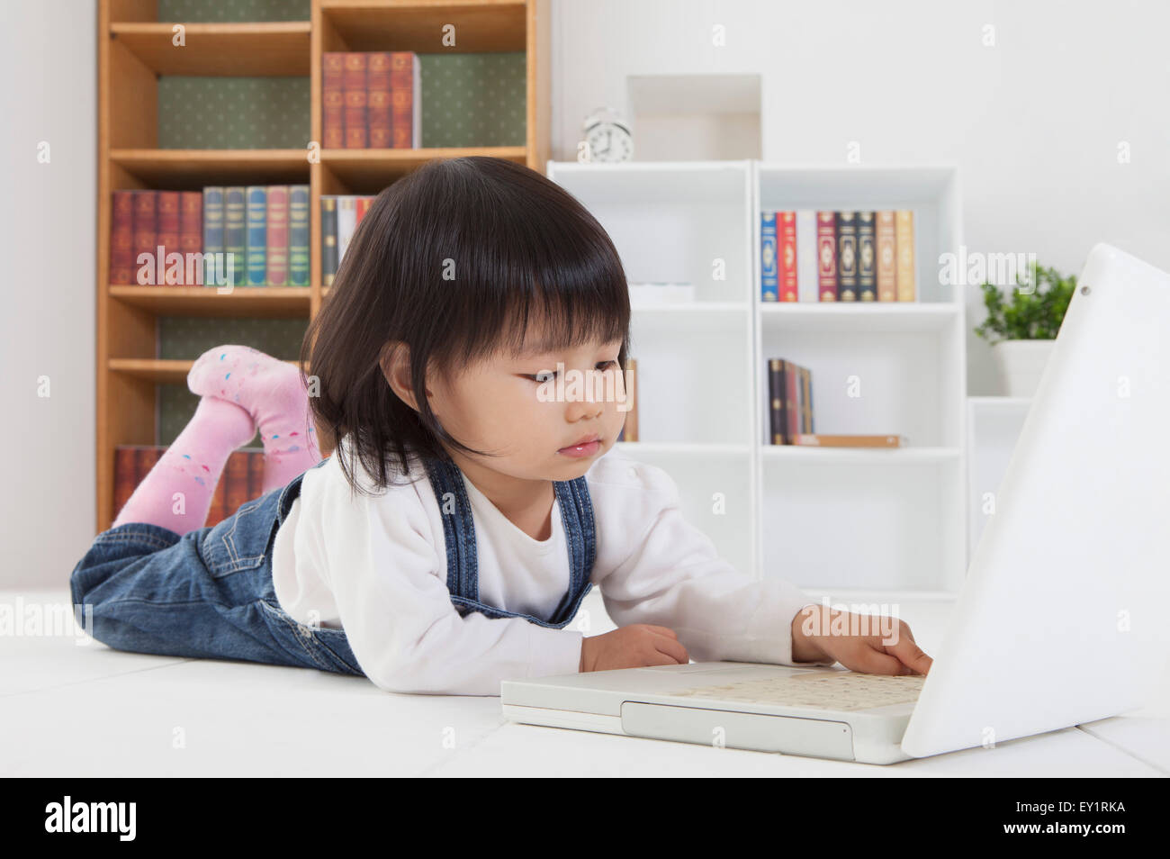 Little girl lying down on front and playing with laptop Stock Photo - Alamy