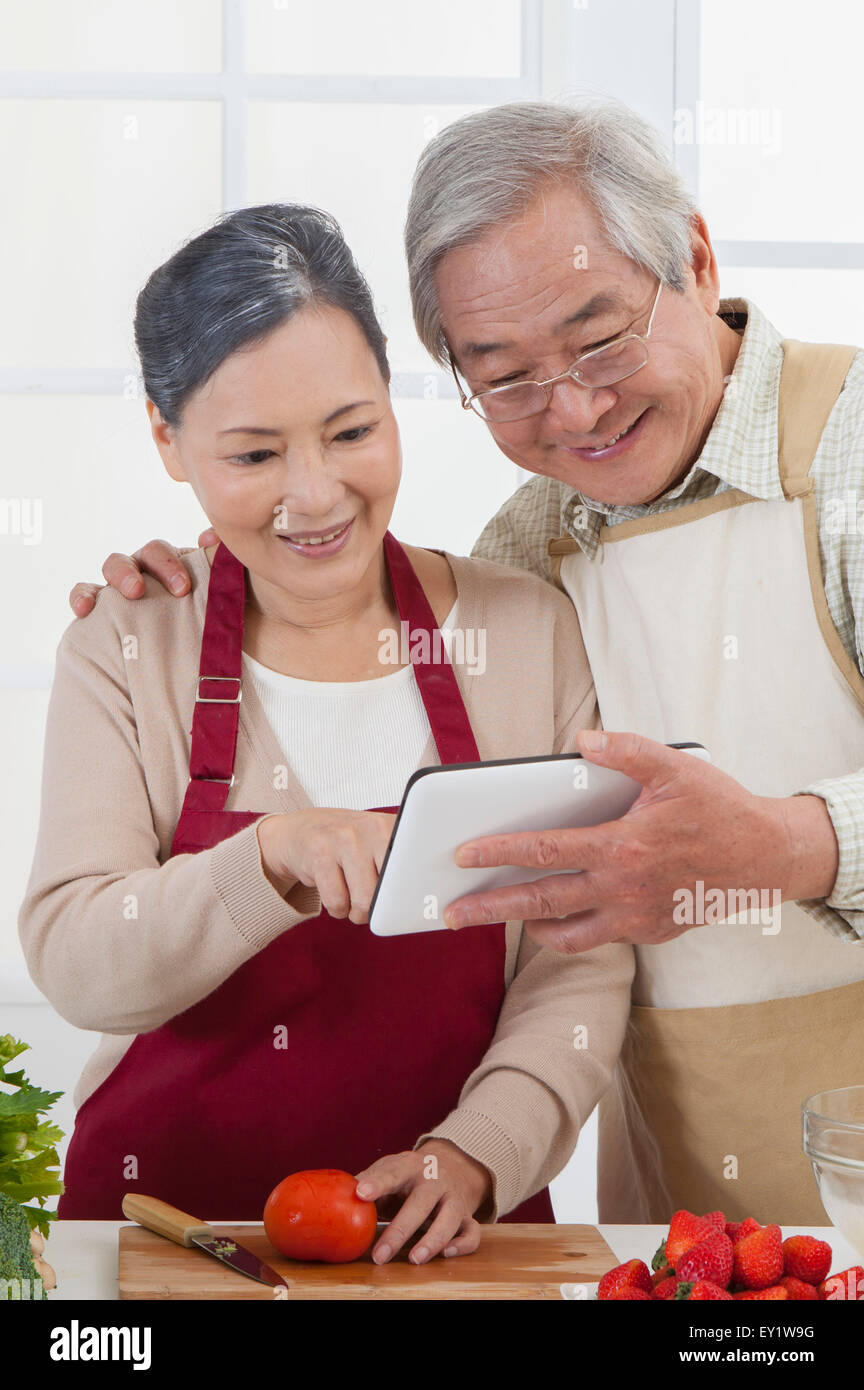 Senior couple holding touch pad in the kitchen and looking with smile ...