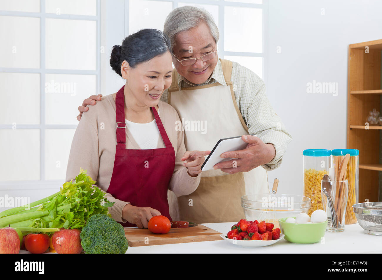 Senior couple holding touch pad in the kitchen and looking with smile ...