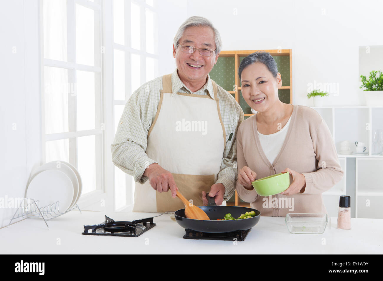 Senior couple cooking in the kitchen and smiling at the camera together ...
