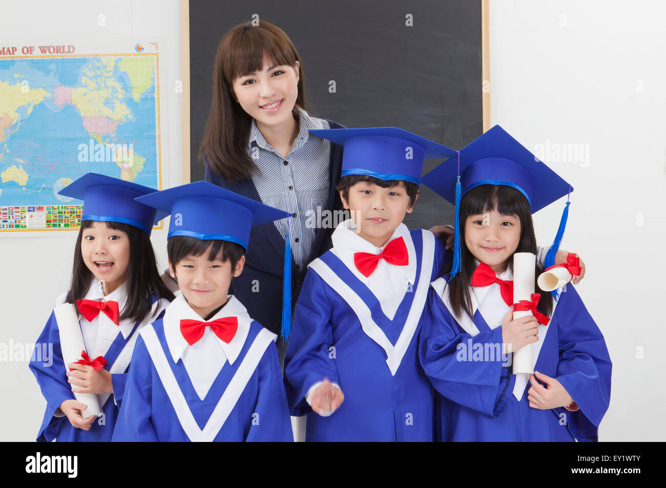 Young teacher and students with graduation gowns smiling at the camera ...