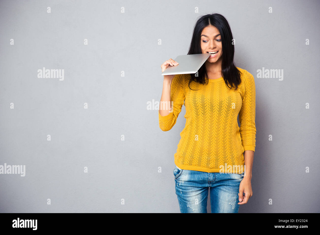 Casual woman biting tablet computer over gray background Stock Photo ...