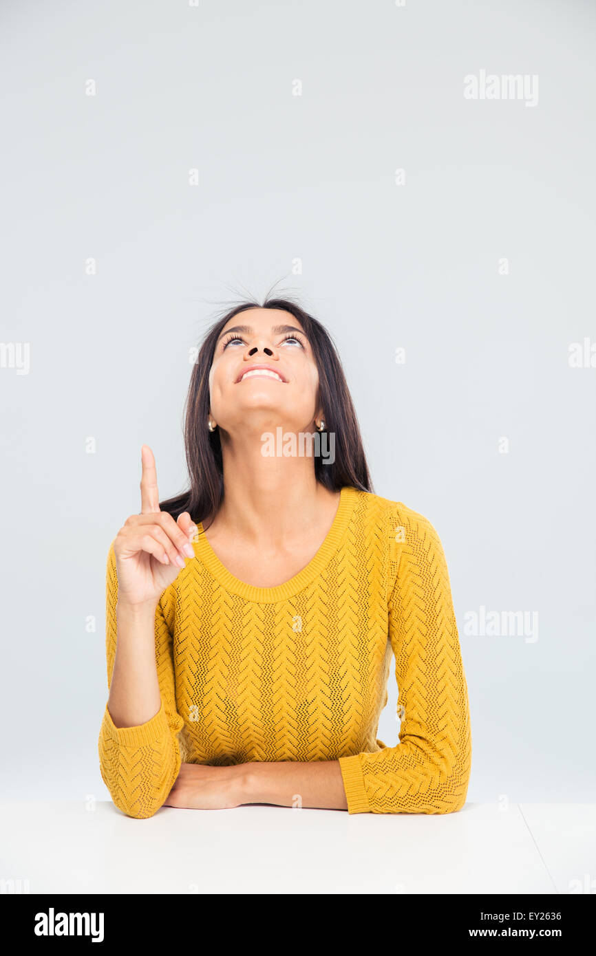 Smiling young woman sitting at the table and pointing finger up at ...