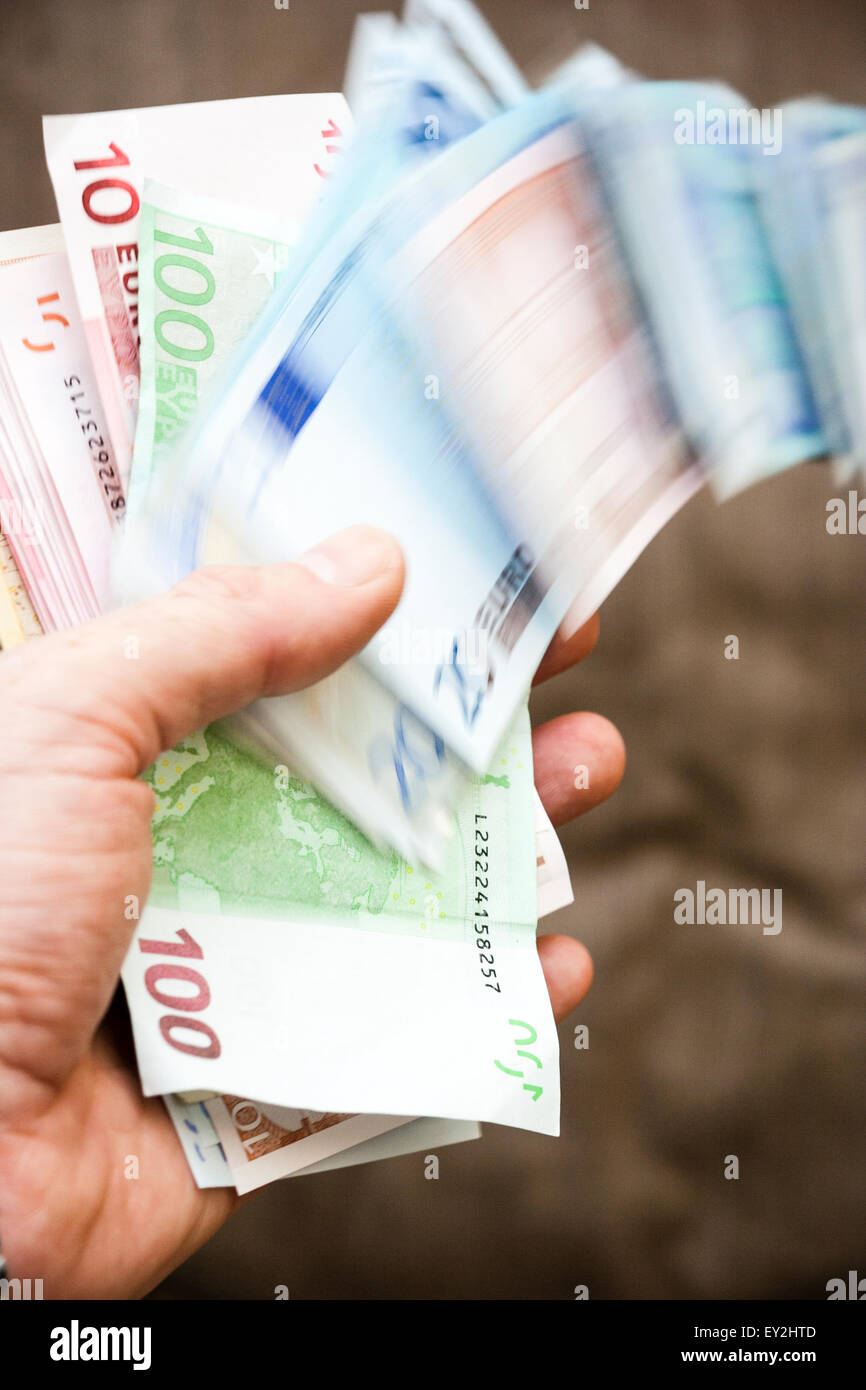 Close up of fingers of hand with wad of Euro banknotes slipping from ...
