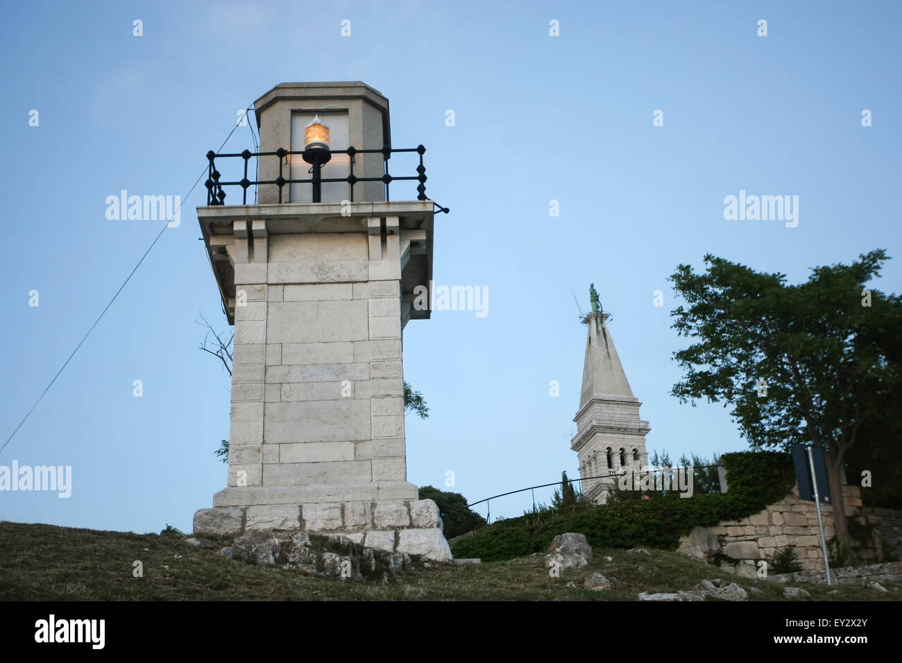 A lighthouse on the shore at sunset with the Saint Eufemia bell tower ...