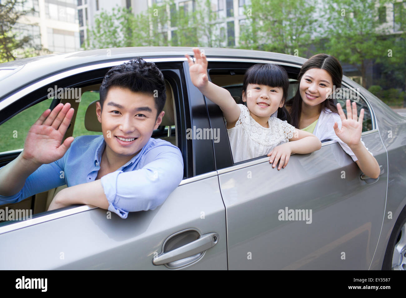 Happy young family waving out of car window Stock Photo - Alamy