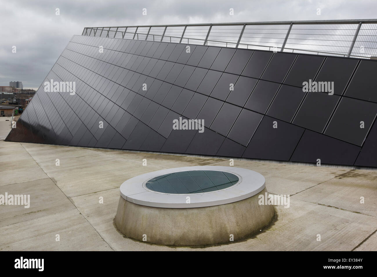 Circular lightwell on concrete roof with sloping upper terrace against ...
