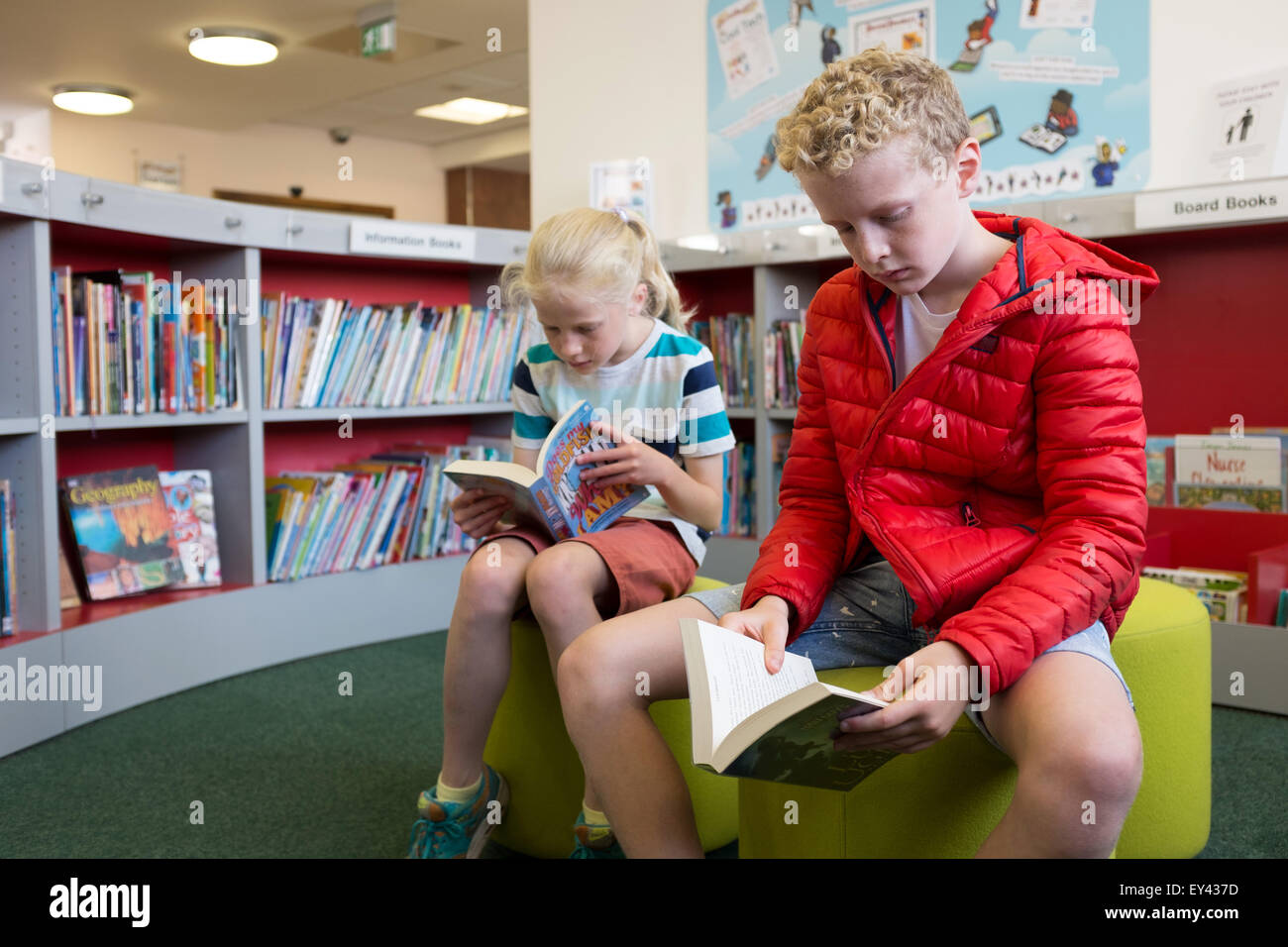Yong boy and girl reading in the children's section of a public library ...