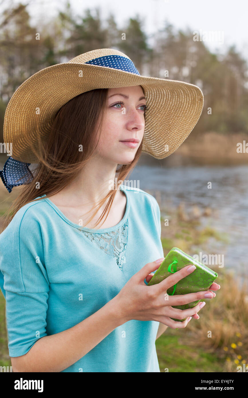 Freckled girl in hat standing with note on the lake in windy weather ...