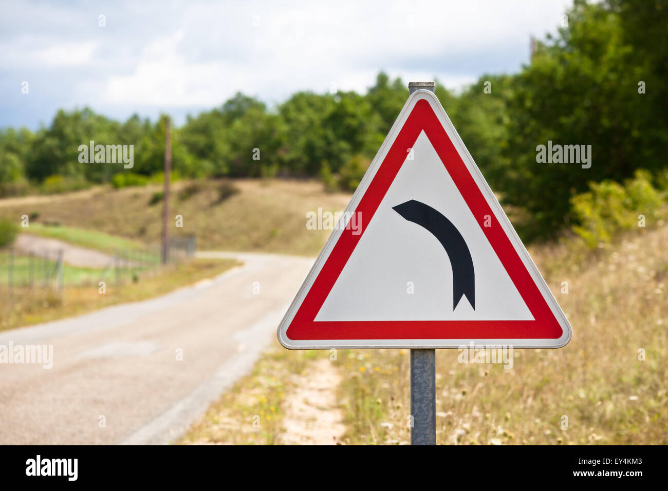Triangular traffic sign indicating road is turning left on a rural road ...