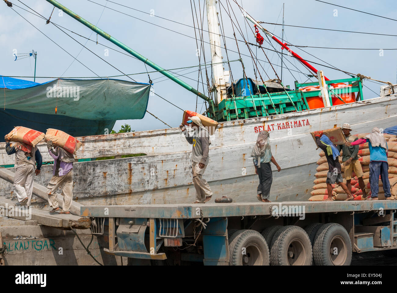 Workers transporting cement sacks from a truck onto a phinisi ship at ...