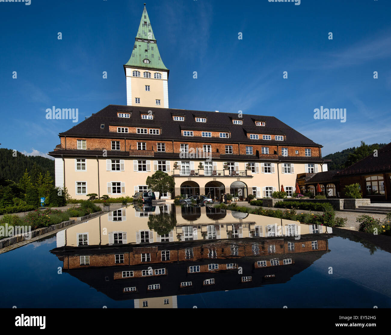 Schloss Elmau Castle Hotel with tower, reflected in the fountain basin ...