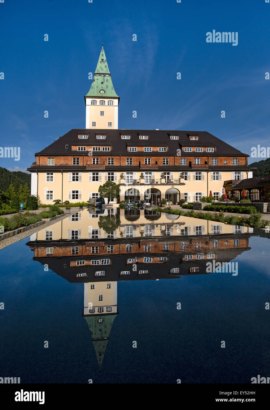 Schloss Elmau Castle Hotel with tower, reflected in the fountain basin ...