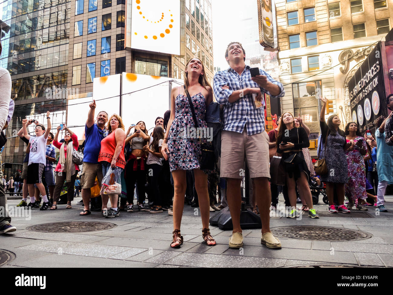 Couple and crowd seeing themselves on huge digital billboard projection ...