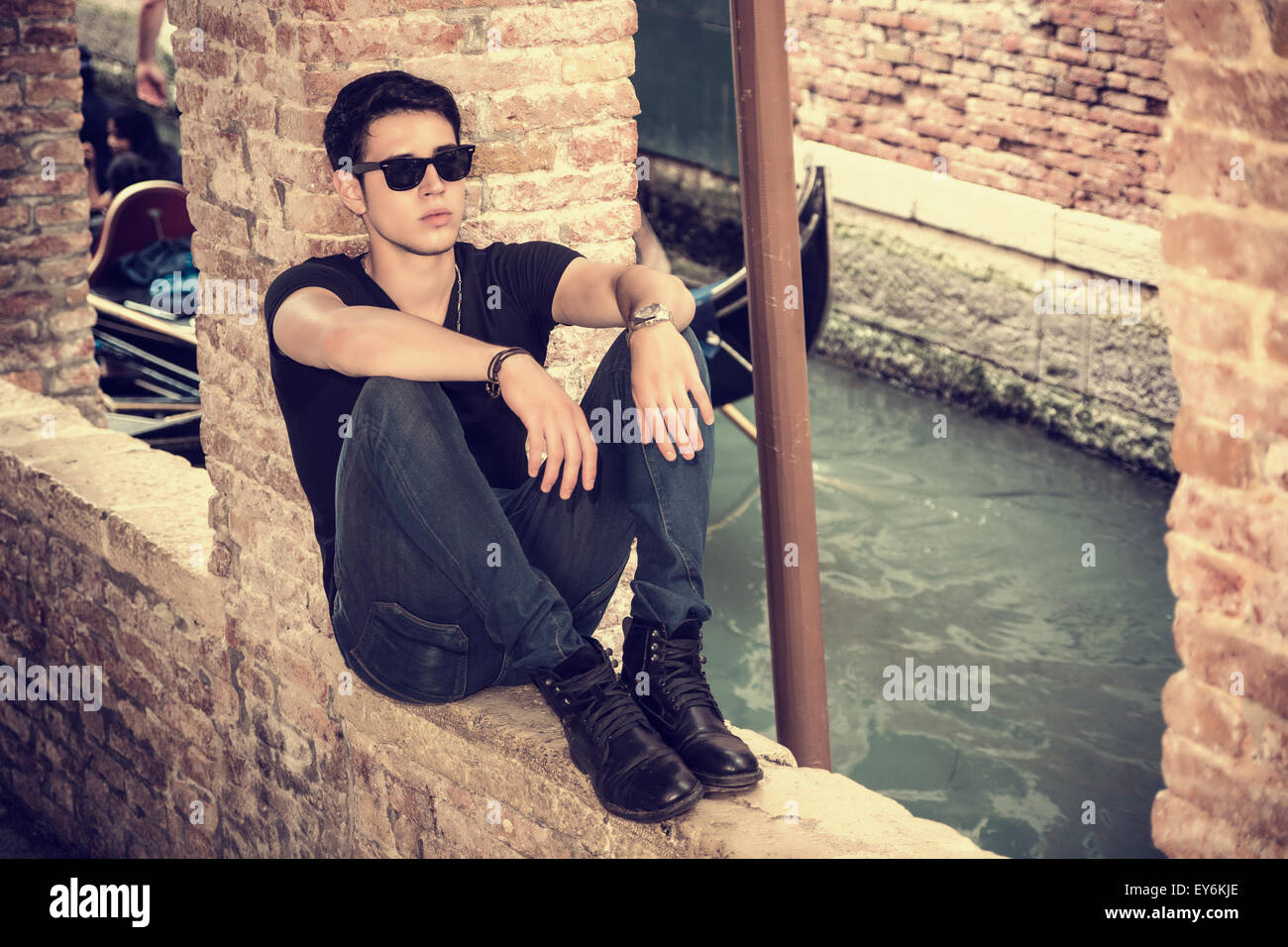 Attractive young man sitting against brick wall, looking in front of ...