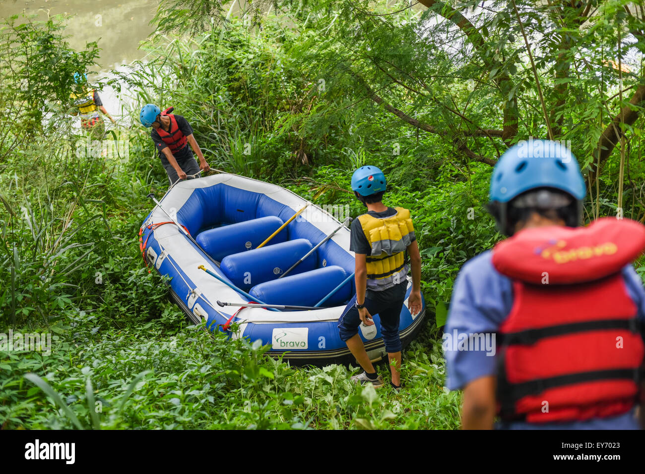 Young men pulling inflatable raft on riverbank Stock Photo - Alamy