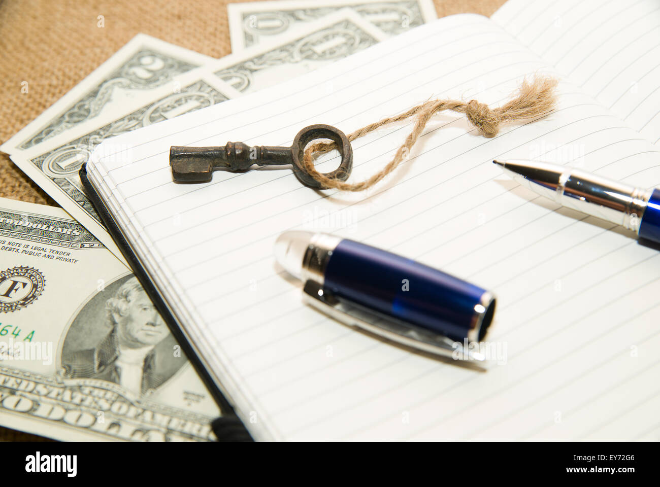 Opened notebook with a blank sheet, pen, key and money on the old ...
