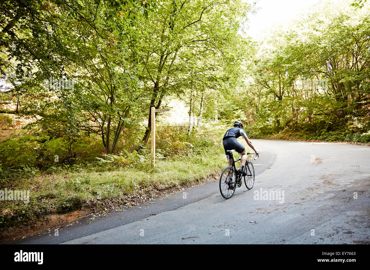 Cyclist rides away up hill on a country road Stock Photo - Alamy