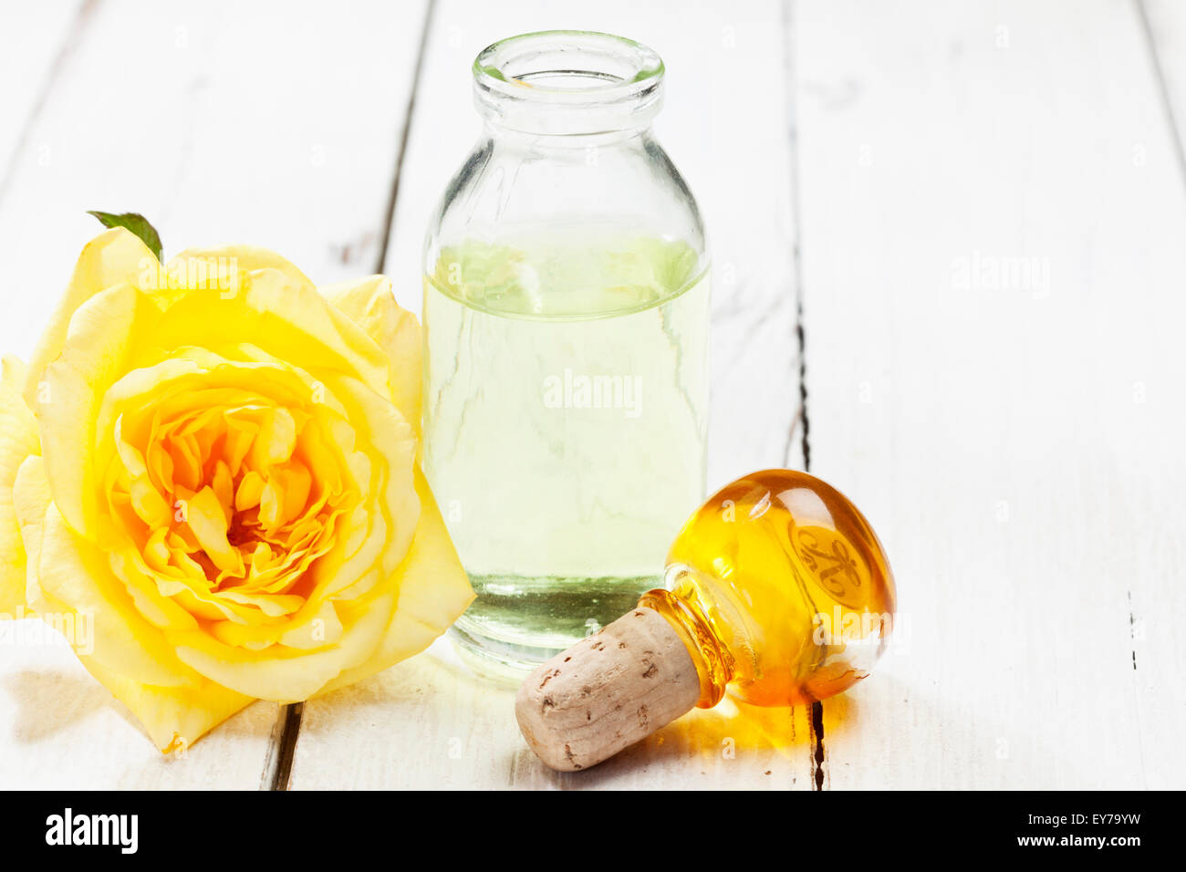 Yellow rose blossom and bottle of fragrance on rustic white wooden ...