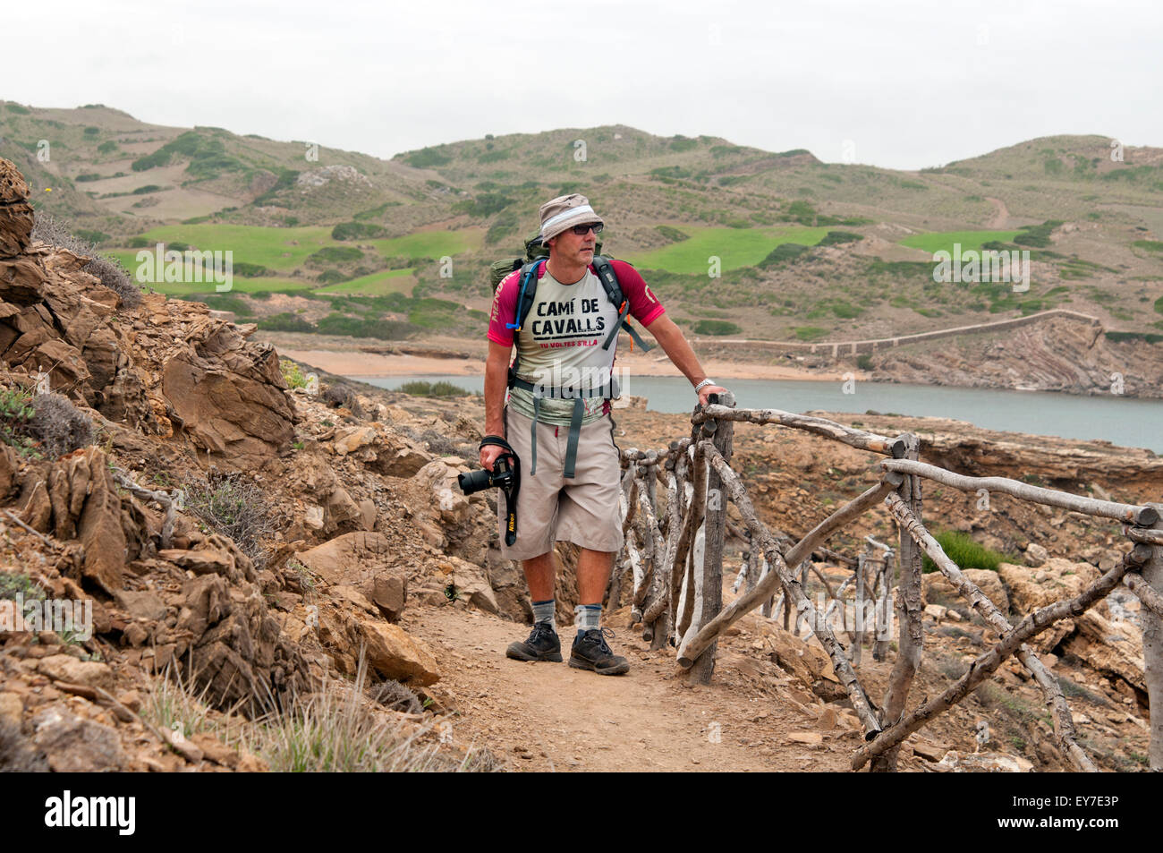 A hiker stops by a fence on the coastal path of the Cami de Cavalls ...