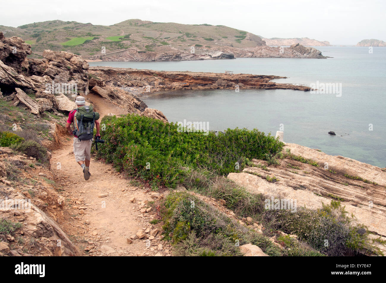 A hiker walks along a rocky northern coastal path of the Cami de ...