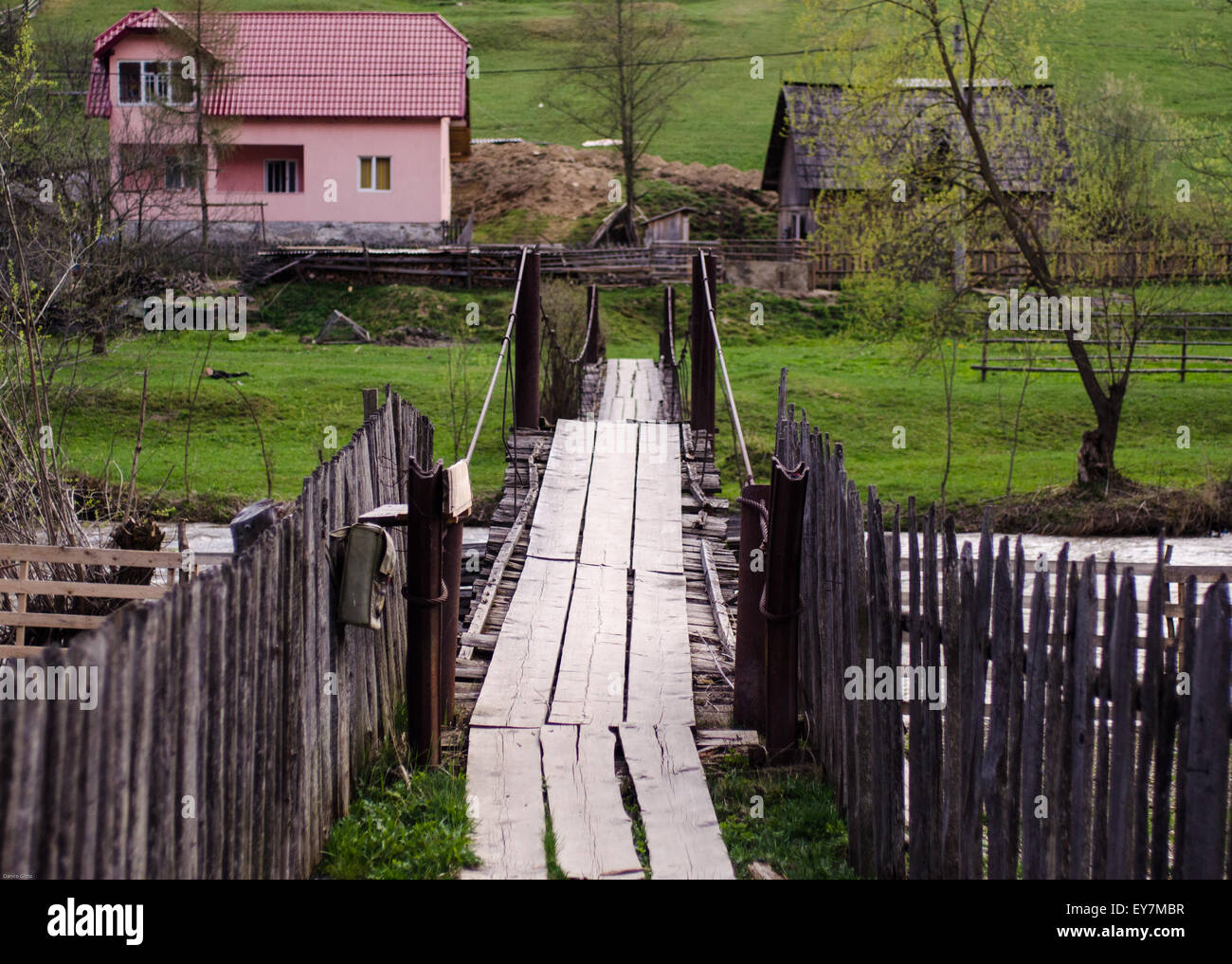Footbridge connecting a rural village to green fields and a river under ...