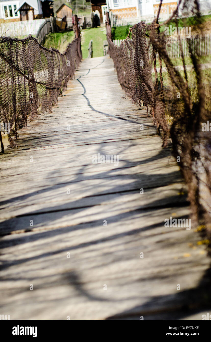 Footbridge connecting a rural village to green fields and a river under ...